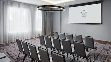 Uma sala de conferências com fileiras de cadeiras, uma tela grande exibindo 'Delta Hotels Marriott Toronto Markham' e um moderno candeeiro de teto.