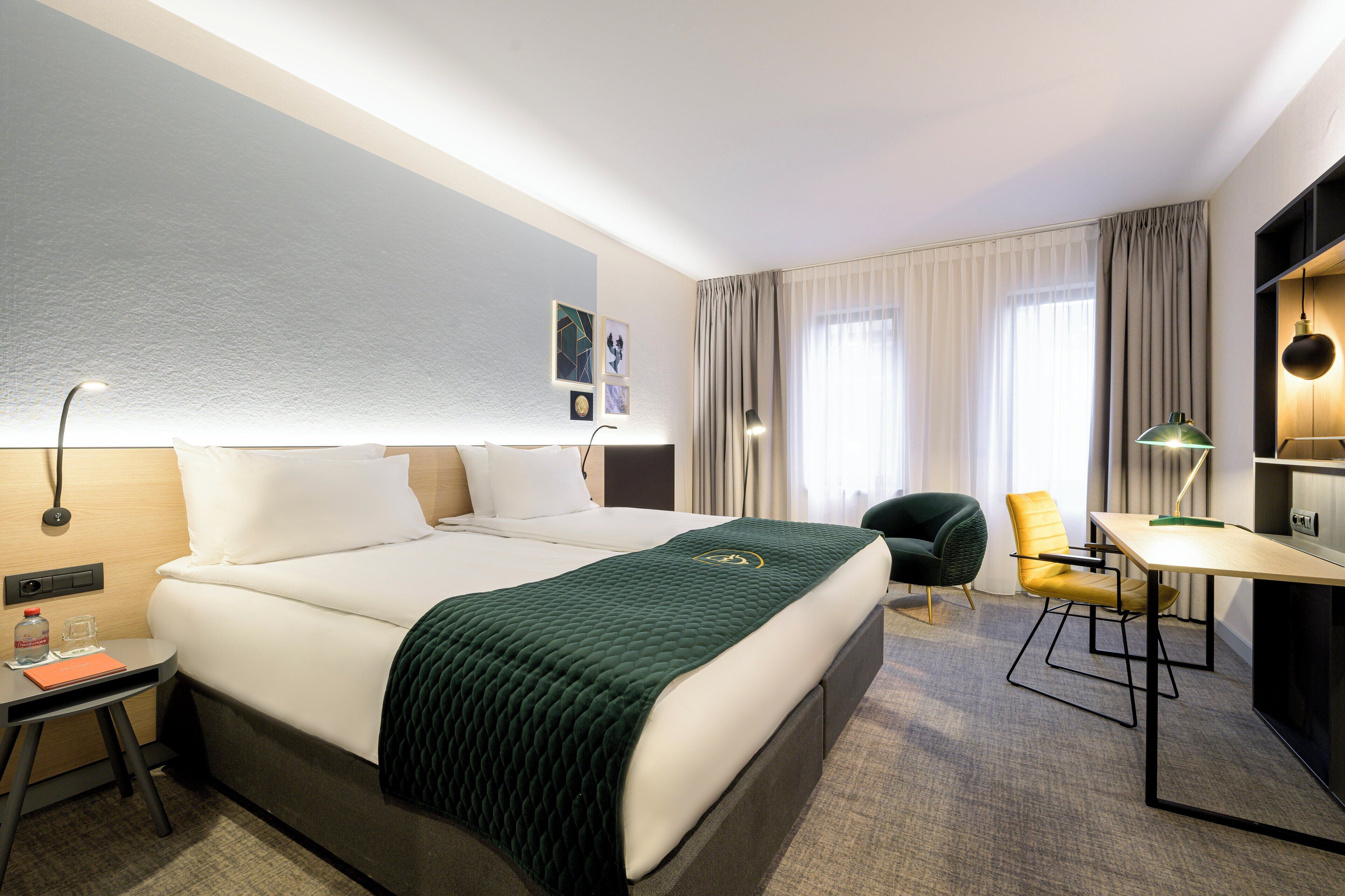 Quarto de hotel com uma cama grande, uma escrivaninha, uma cadeira e uma pequena mesa com abajur.