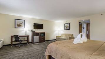 Quarto de hotel com cama, escrivaninha com cadeira, televisão, sofá e quadro na parede.