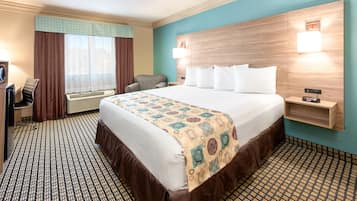 Quarto de hotel com uma cama grande, uma secretária com cadeira, uma janela com cortinas e uma estante fixada na parede.