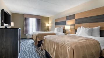 Quarto de hotel com duas camas, televisão, secretária e janela com cortinas.