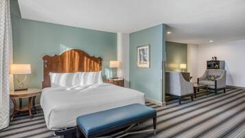 Quarto de hotel com uma cama grande, mesas de cabeceira, um banco, uma cadeira e uma pequena mesa com abajur.