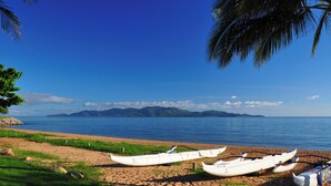 Uma praia com canoas dispostas na areia, céu azul límpido e montanhas ao longe.
