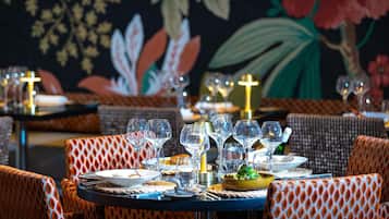 Interior de restaurante com mesas redondas, cadeiras com padrão laranja e arte floral nas paredes.