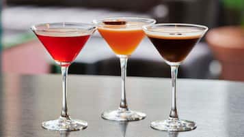 Três copos de martini com bebidas de cores diferentes sobre uma mesa.