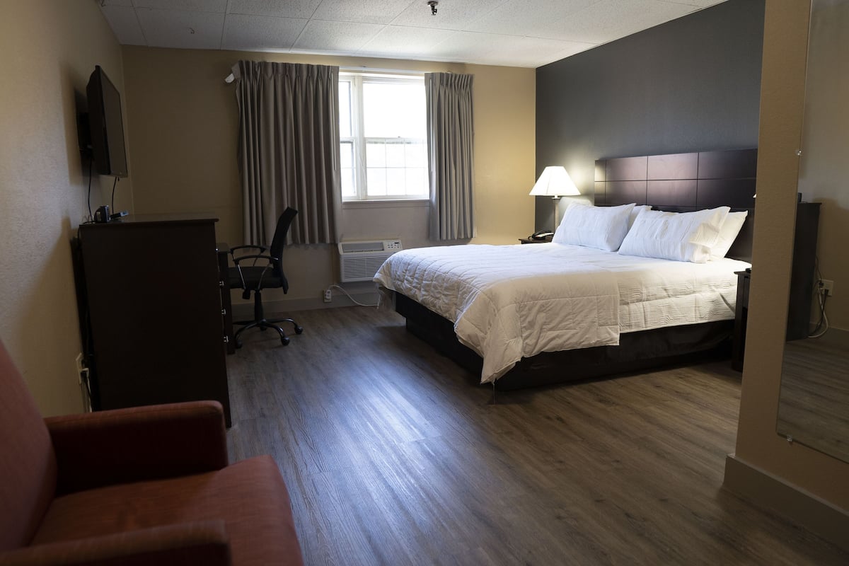 Quarto de hotel com cama, escrivaninha, cadeira, televisão e janela com cortinas.