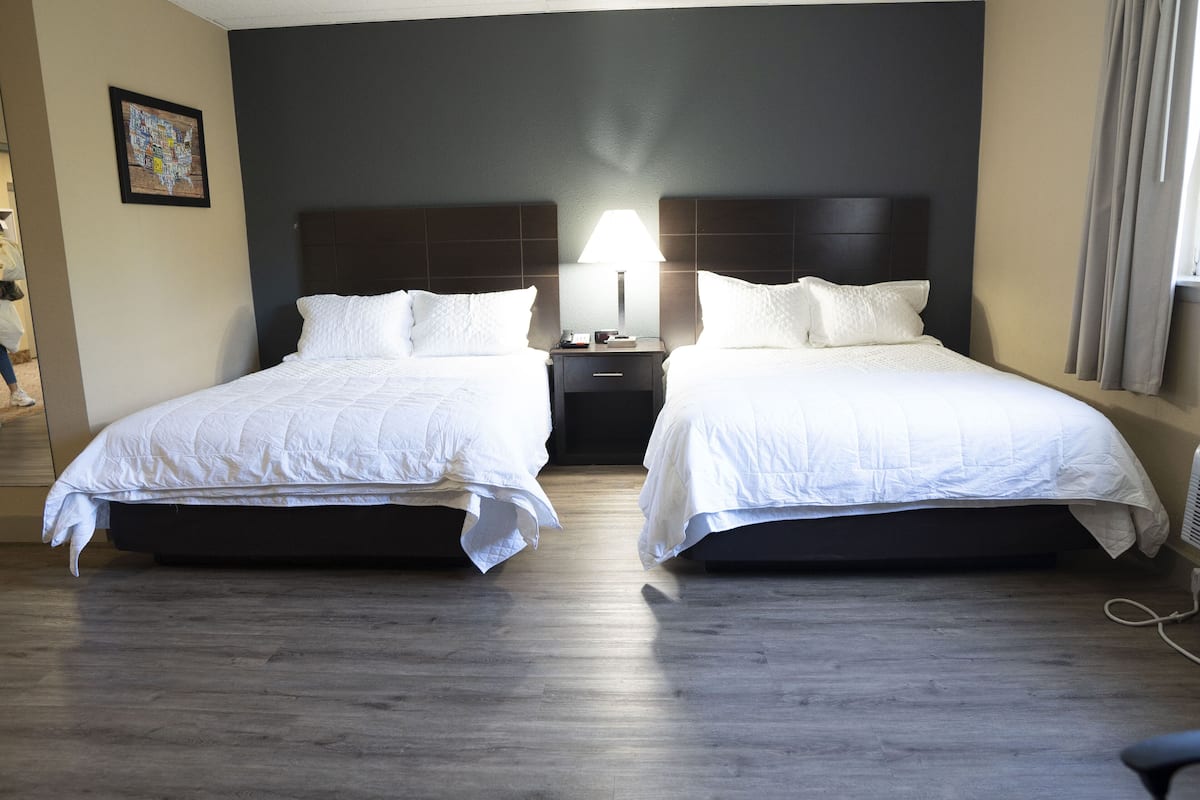 Quarto de hotel com duas camas, uma mesa de cabeceira, um abajur e um quadro na parede.