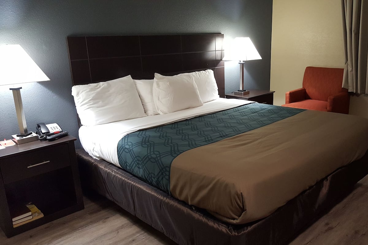 Quarto de hotel com uma cama grande, duas mesas de cabeceira, uma cadeira, um abajur e um aparelho de ar condicionado.