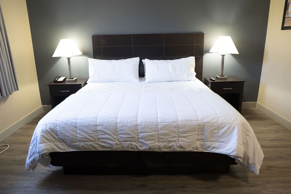 Uma cama bem arrumada com um edredom branco, duas mesas de cabeceira com luminárias e uma cabeceira escura.