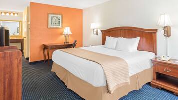 Quarto de hotel com uma cama grande, uma escrivaninha, uma cadeira, uma luminária de mesa, uma mesinha de cabeceira com abajur e um telefone.