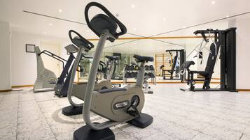 Uma academia com aparelhos de cardio, equipamentos de musculação e um espelho grande na parede.