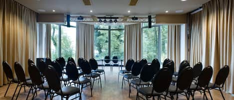 Uma sala de conferências com uma mesa comprida e cadeiras, janelas grandes com cortinas e teto com iluminação embutida.