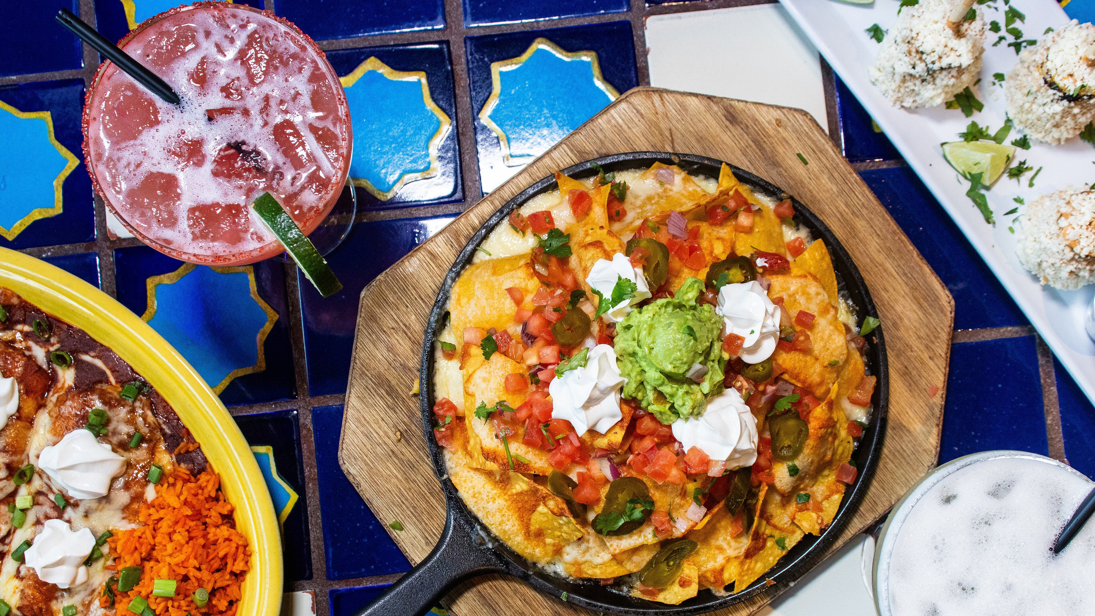 Uma frigideira de nachos com cobertura, uma tigela de arroz e uma margarita em uma superfície azulejada.
