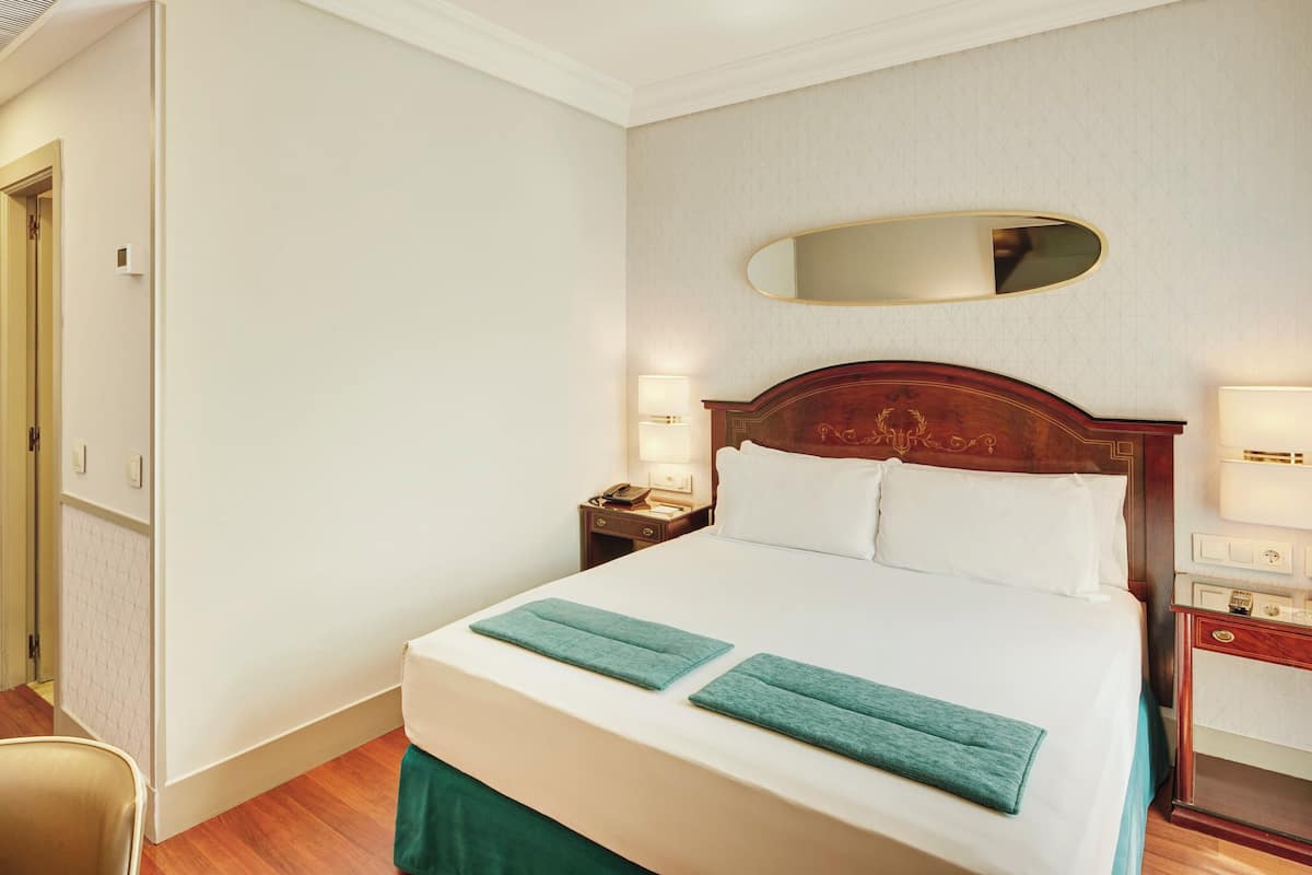Quarto de hotel com cama, mesa de cabeceira, espelho, escrivaninha e cadeira.