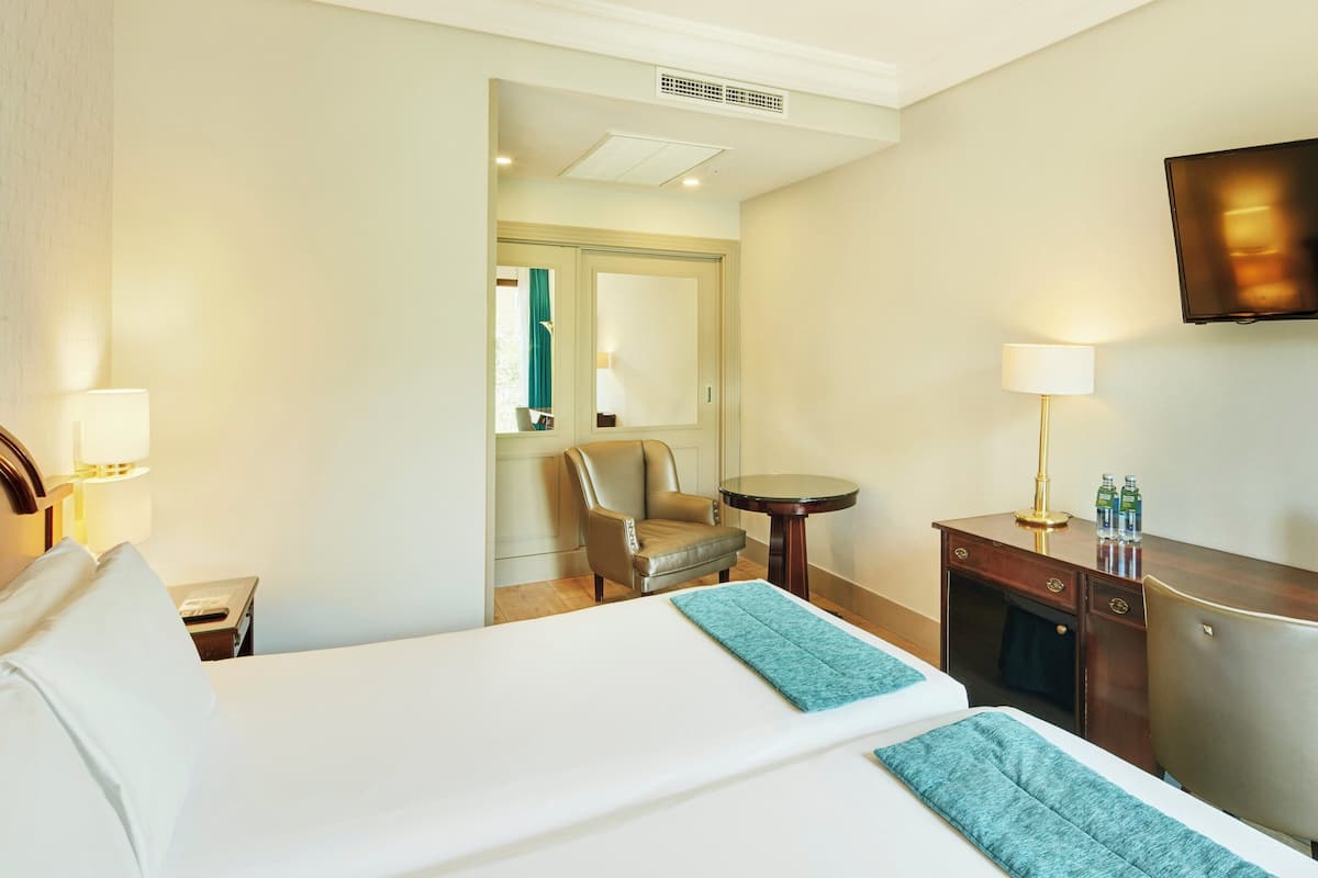Quarto de hotel com cama, escrivaninha, cadeira, televisão e janela com cortinas.