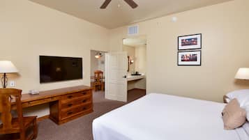 Quarto de hotel com cama, escrivaninha, cadeira, televisão e duas fotos emolduradas na parede.