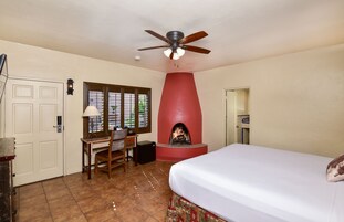 Um quarto com uma cama, uma escrivaninha, uma cadeira, uma lareira vermelha e um ventilador de teto.