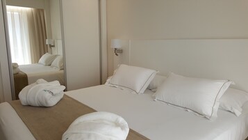Quarto de hotel com cama grande, duas almofadas, mesa de cabeceira, abajur e espelho.