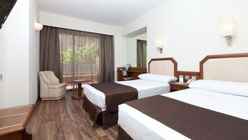 Quarto de hotel com duas camas, uma escrivaninha, uma cadeira e uma mesinha.