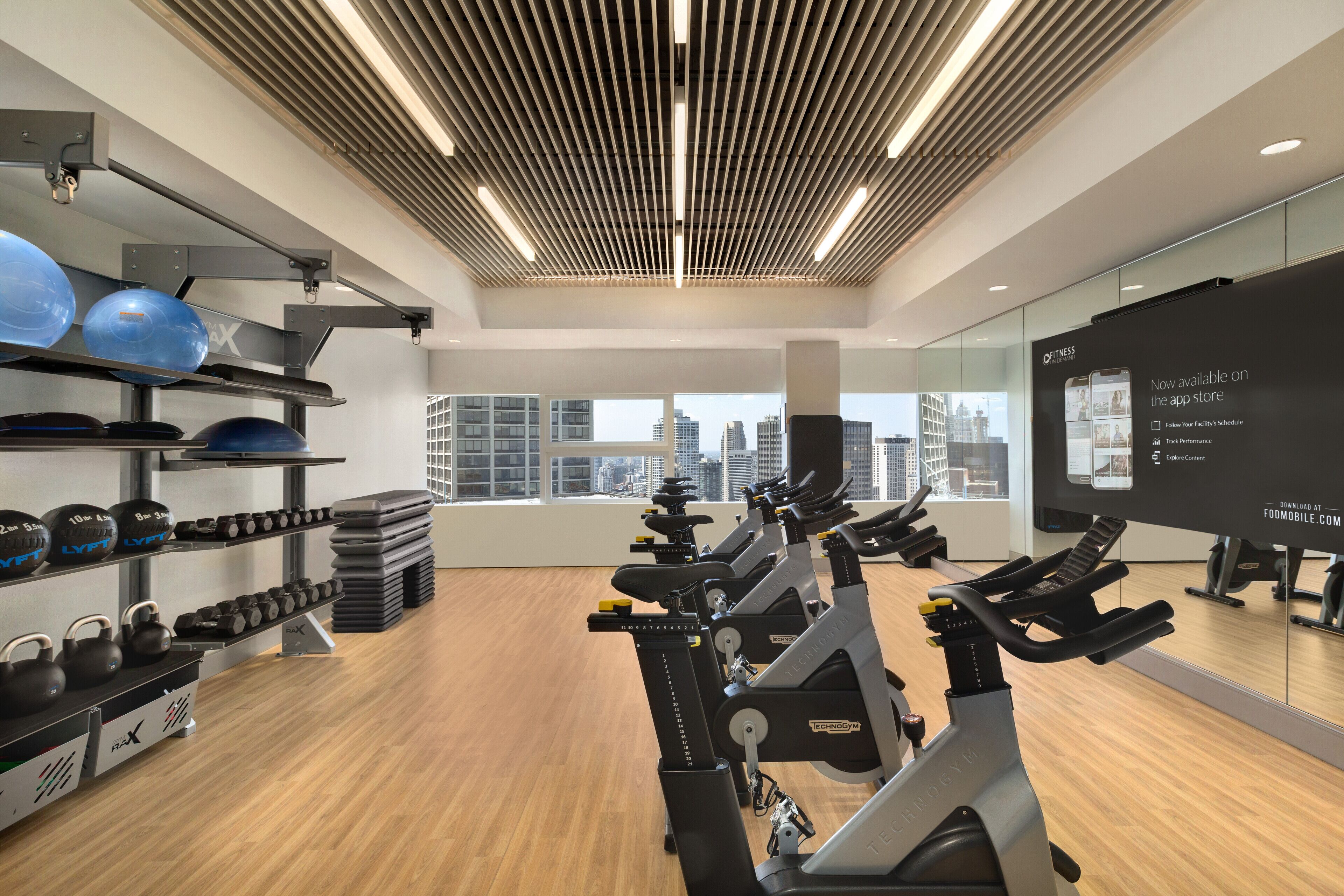 Uma academia moderna com equipamentos de exercício, vista para a cidade e um espelho grande.
