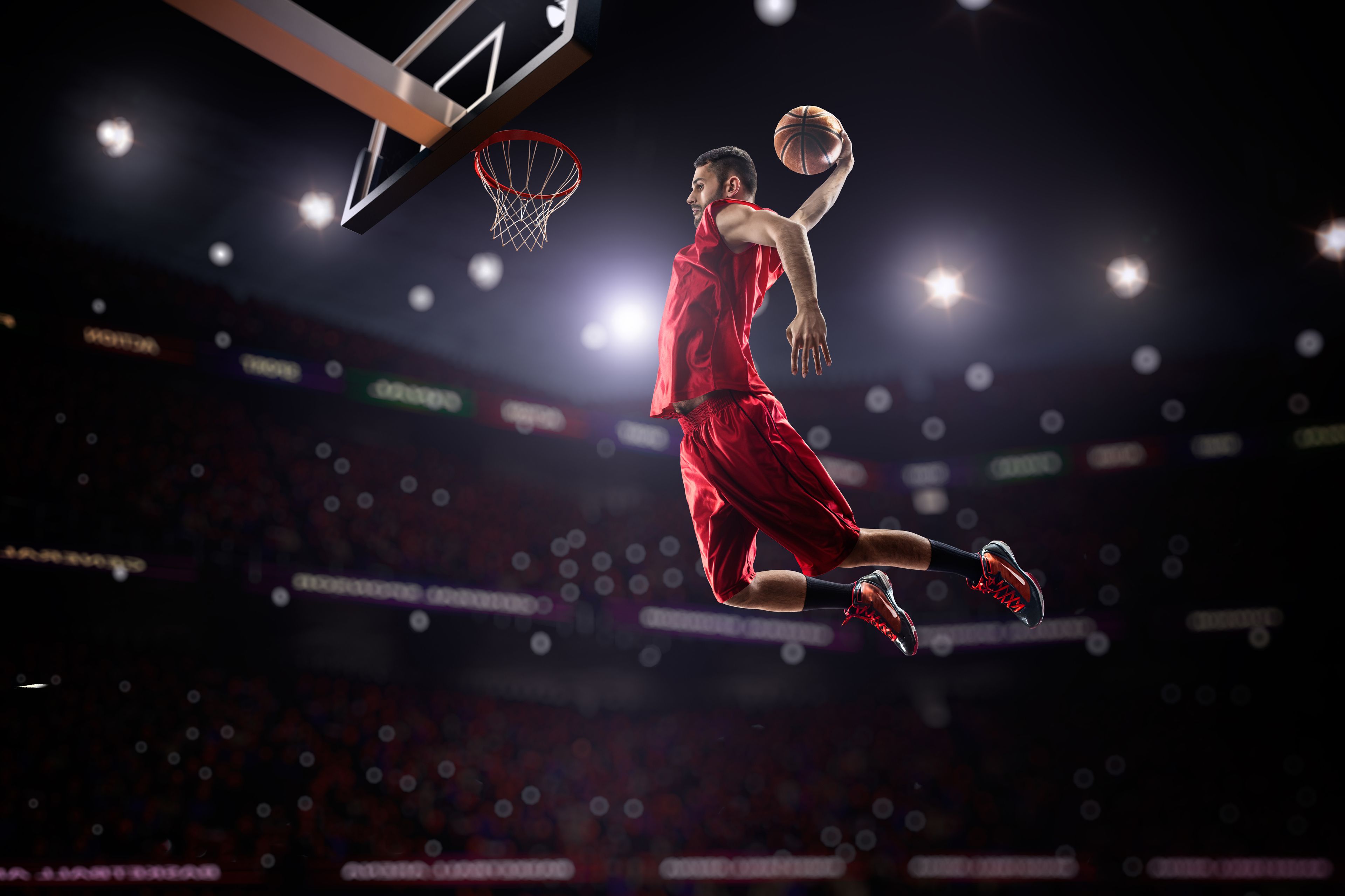 Um jogador de basquete no ar, enterrando a bola em uma arena coberta bem iluminada.