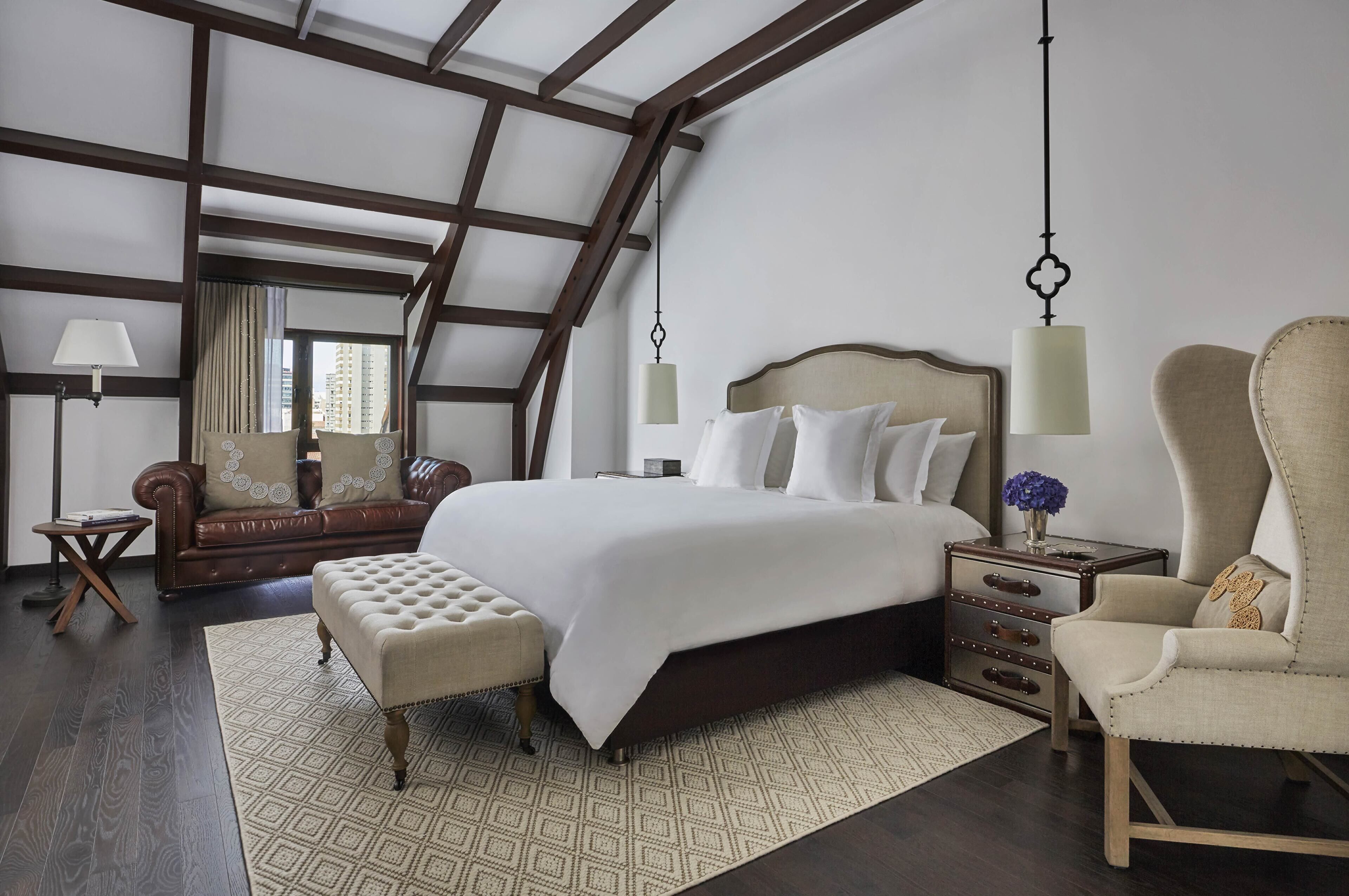 Quarto com cama grande, sofá, cadeira, mesa de cabeceira e abajur.