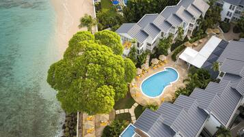 Vista aérea de um resort com piscina, vários edifícios e uma grande árvore.