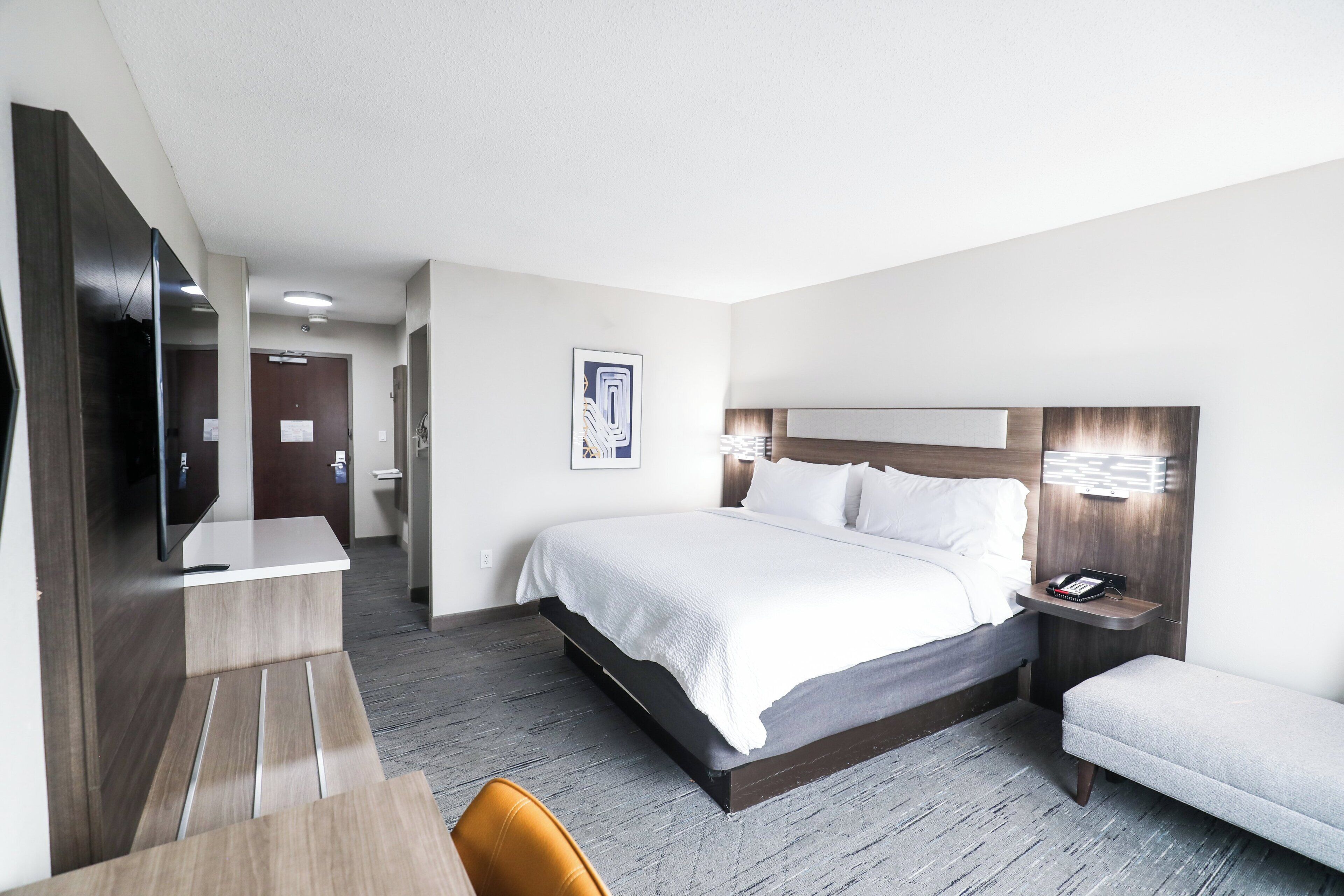 Quarto de hotel moderno com uma cama grande, uma mesa, uma cadeira e uma televisão.