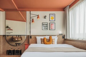 Quarto moderno com uma cama grande, mesa de cabeceira com abajur, espelho e obras de arte emolduradas na parede.