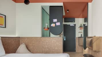 Quarto de hotel com uma cama, uma planta pequena, uma porta e um espelho.