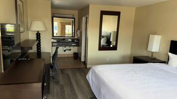 Quarto de hotel com uma cama, uma escrivaninha, uma cadeira, um espelho, uma mesa de cabeceira e um abajur.