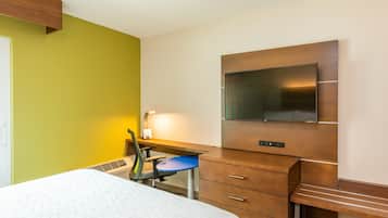 Quarto de hotel com uma cama, uma escrivaninha com cadeira, televisão fixada na parede e um armário de madeira.