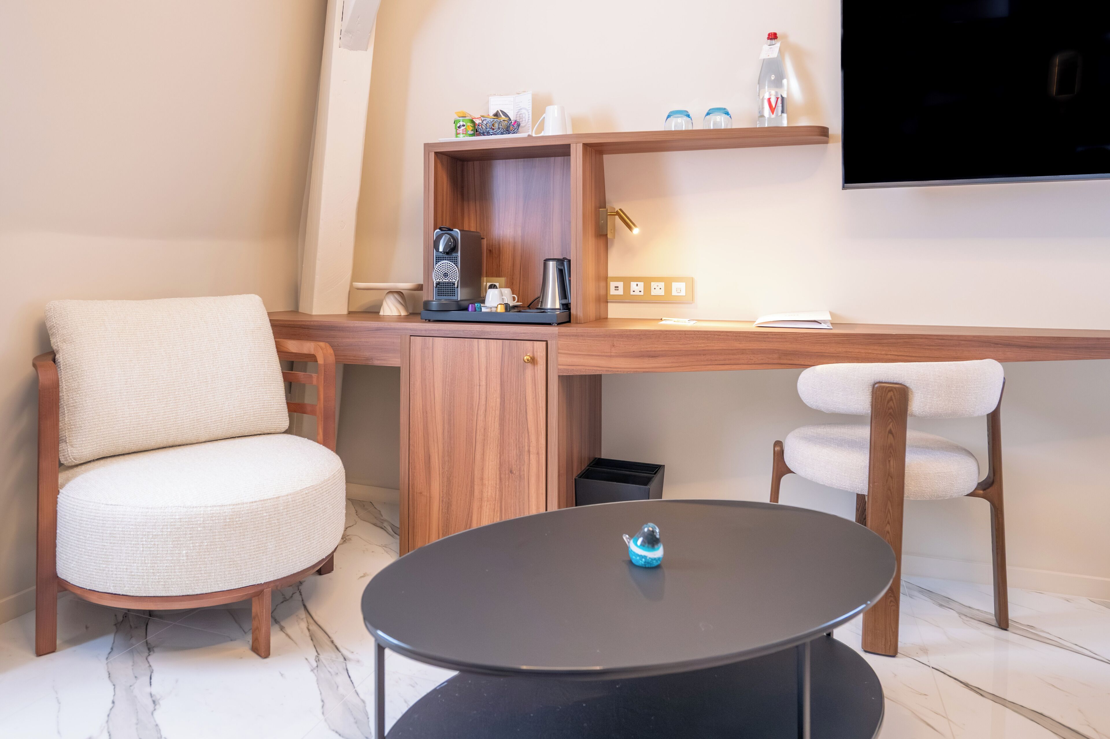Quarto moderno com escrivaninha de madeira, duas cadeiras, uma mesa redonda e uma TV fixada na parede.