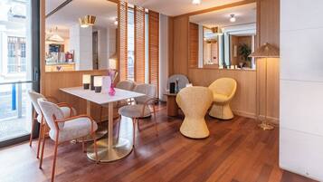 Quarto de hotel moderno com piso de madeira, uma mesa de jantar com cadeiras, um espelho grande e um abajur.