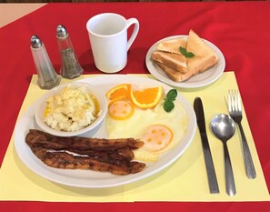 Prato de café da manhã com ovos, torrada e bacon, uma xícara e saleiro e pimenteiro sobre uma mesa.