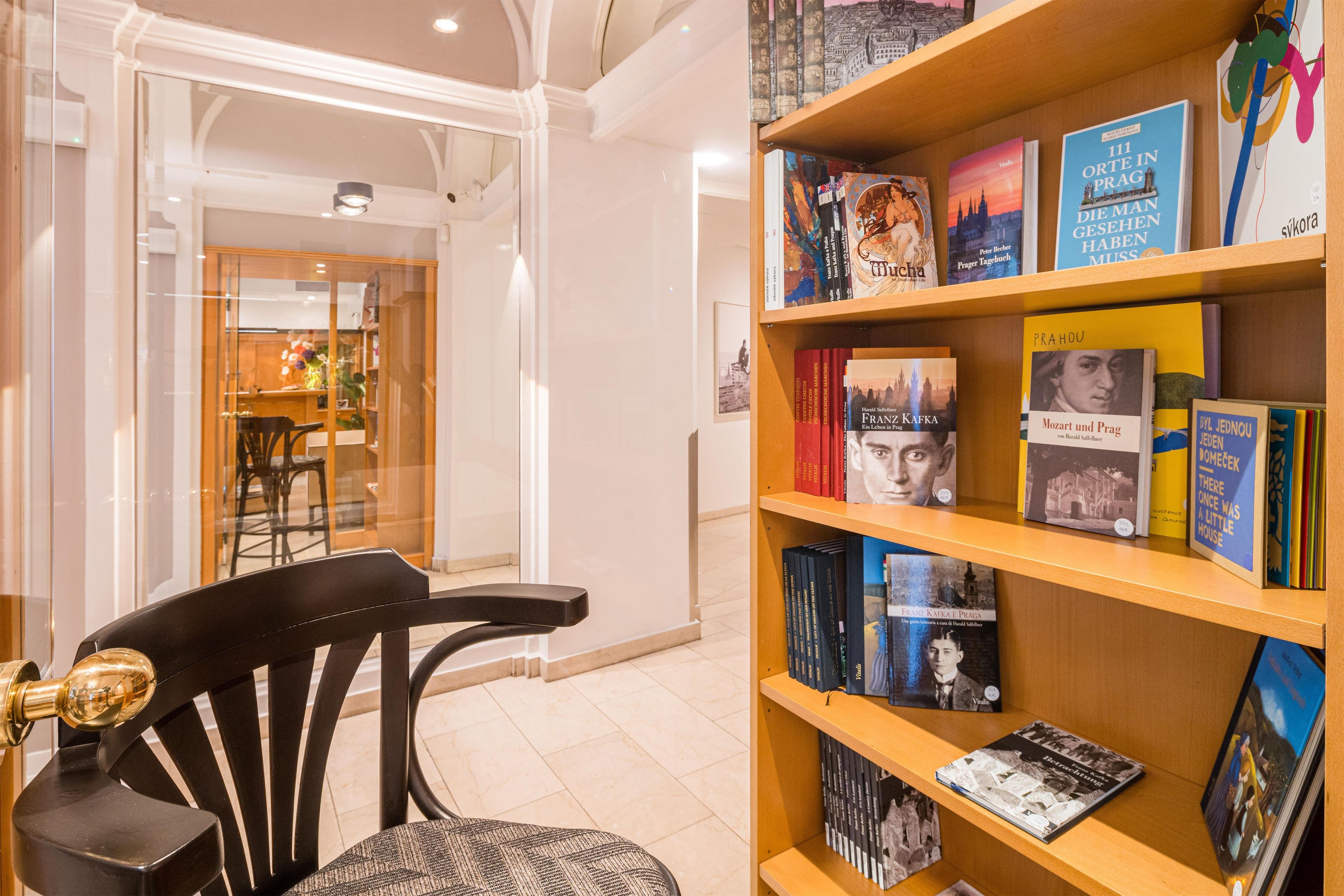 Interior de biblioteca com estantes, uma cadeira preta e uma mesa com abajur.