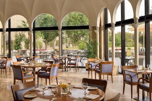 Uma sala de jantar ampla com várias mesas e cadeiras, grandes janelas com vista para o exterior e um interior bem iluminado.