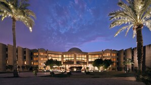 Um hotel com fachada simétrica, grandes janelas e palmeiras em primeiro plano.