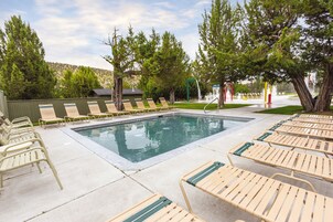 Uma área de piscina com espreguiçadeiras e um pequeno edifício ao fundo.