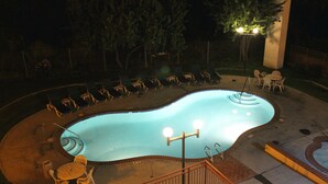 Piscina com espreguiçadeiras e um pequeno espaço com mesa, cercada por um muro de tijolos baixo e um corrimão de metal.