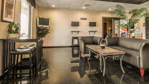 Um lobby com um sofá de couro preto, uma mesinha, uma TV fixada na parede e um aviso de 'ECONOMIZE ÁGUA'.