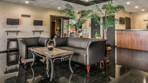 Um lobby com sofá de couro preto, mesa de centro de madeira e balcão de recepção.