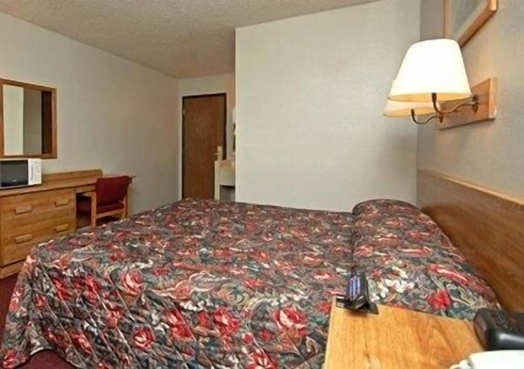 Quarto de hotel com cama, escrivaninha, cadeira, abajur e espelho.