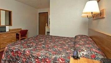 Quarto de hotel com cama, escrivaninha, cadeira, abajur e espelho.