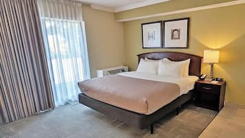 Quarto de hotel com uma cama grande, uma mesa de cabeceira com abajur e uma janela com cortinas.