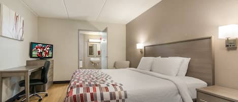 Quarto de hotel com cama, escrivaninha, cadeira, televisão e banheiro visível por uma porta aberta.
