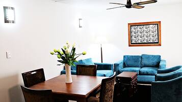 Uma sala de jantar com uma mesa e cadeiras de madeira, um vaso com flores, um sofá azul e um quadro na parede.