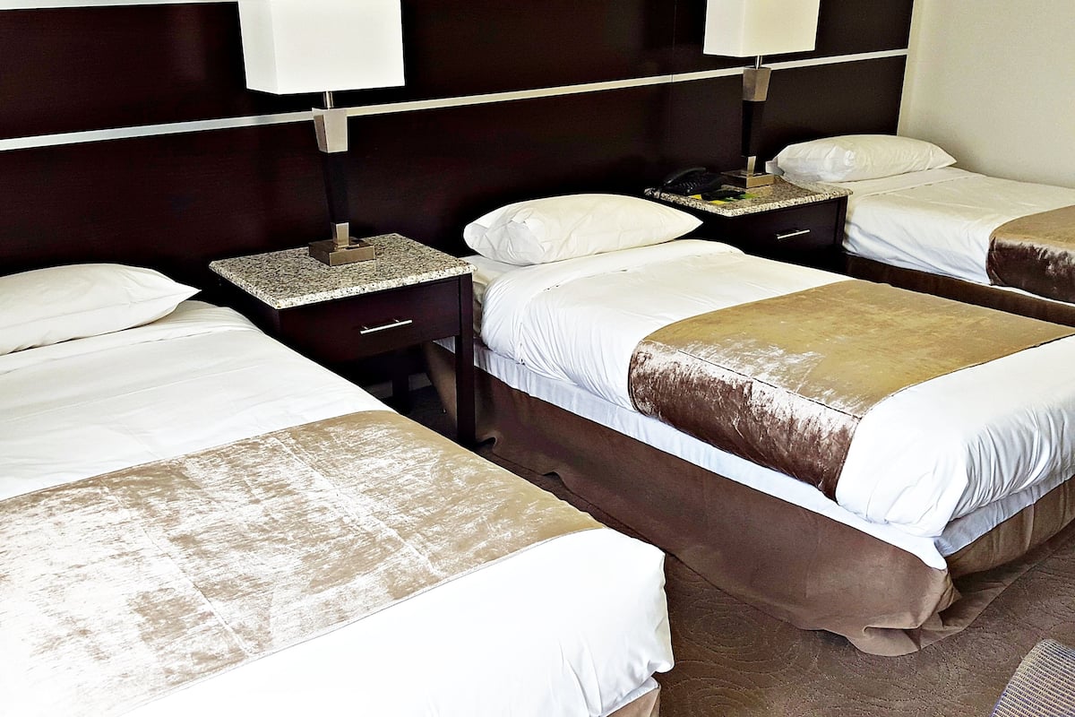 Quarto de hotel com quatro camas de solteiro, cada uma com travesseiro e mesa de cabeceira.