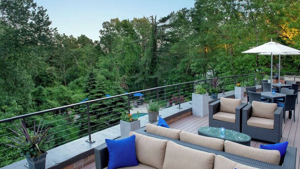 Uma área de pátio externa com sofás, uma mesa de jantar e um grande guarda-sol.