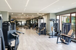 Uma academia moderna com diversos equipamentos de exercício, um espelho e vista para o exterior através de amplas janelas.